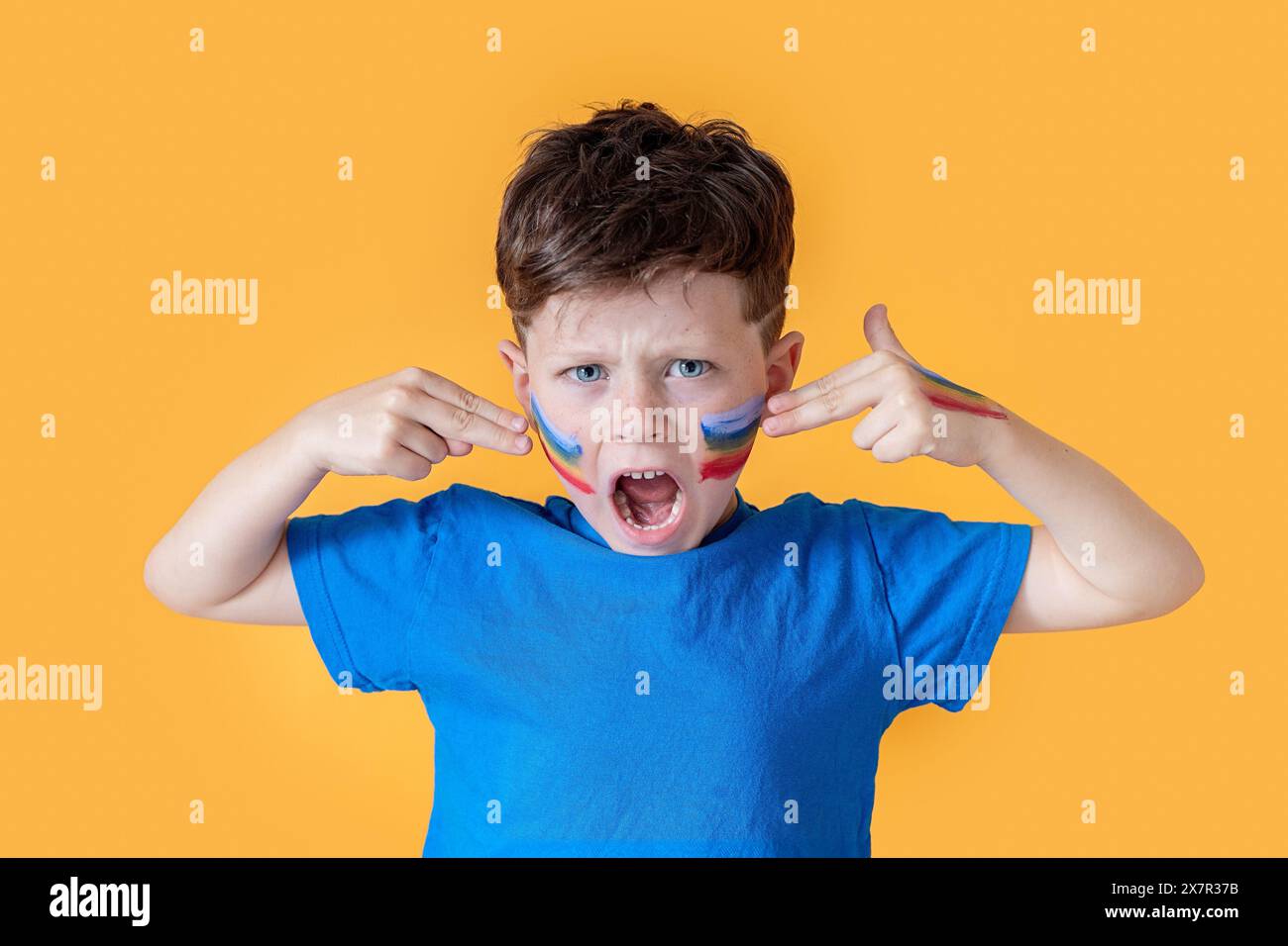 A young boy in a blue shirt, with face paint in blue and red stripes ...