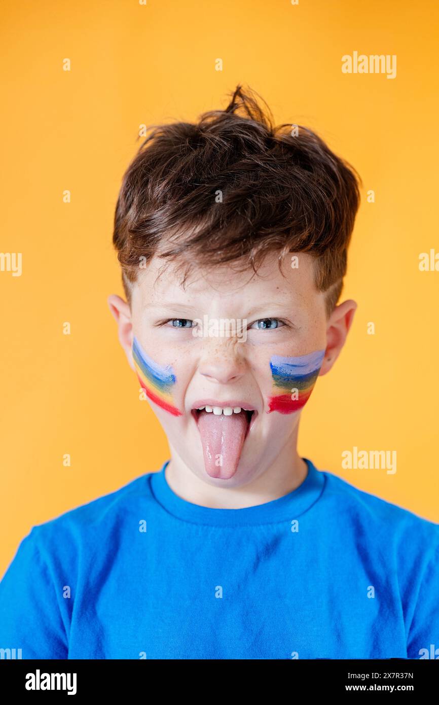 A playful young boy wearing a vivid blue shirt sticks out his tongue ...
