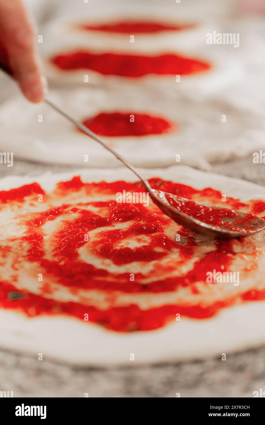 An anonymous chef in a pizzeria spreads tomato sauce on pizza dough ...