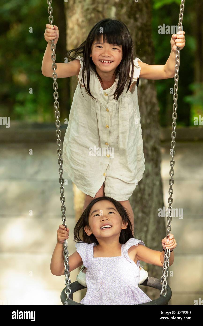 Two Asian sisters enjoy a playful moment on a swing set in a European ...