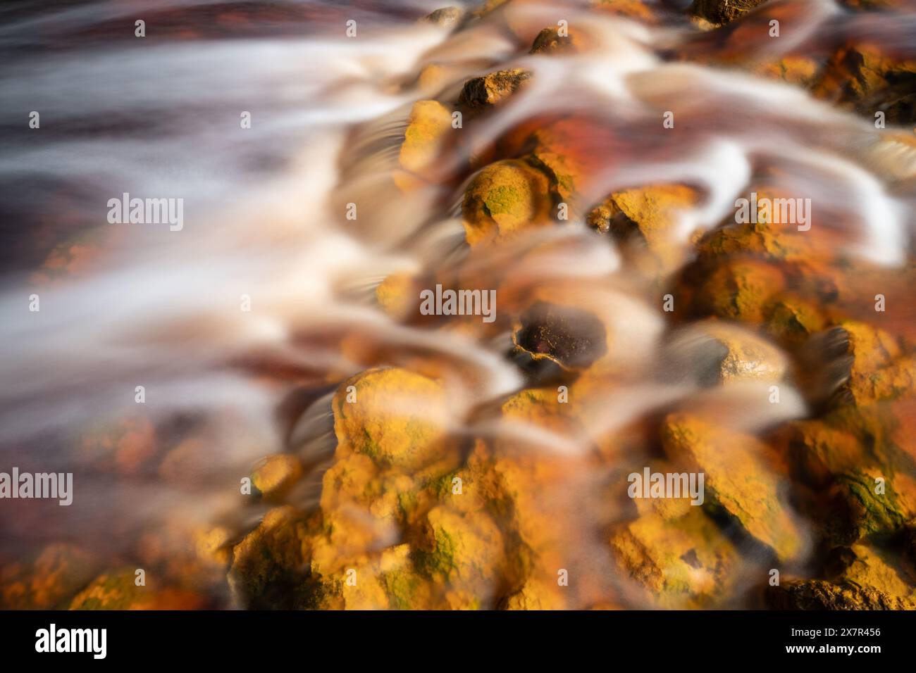 A close-up photo captures the dynamic flow of water over vivid, orange ...