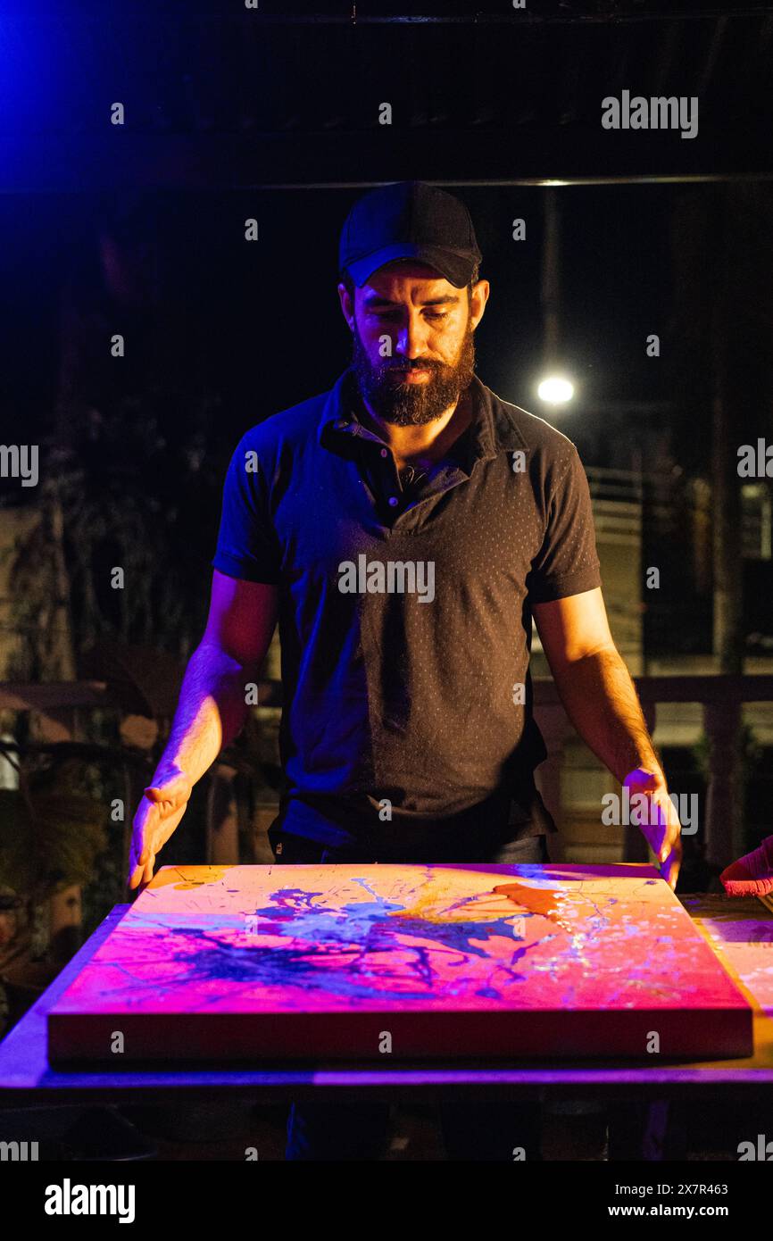 A contemplative focused male artist stands over his vibrant painting in ...