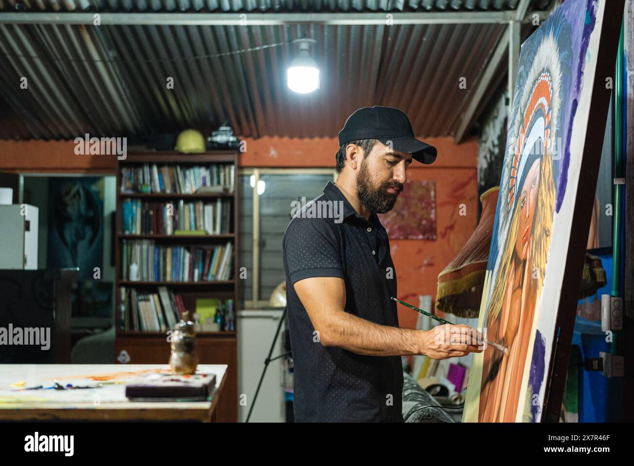Side view of a Latin American male artist intently paints on a canvas ...