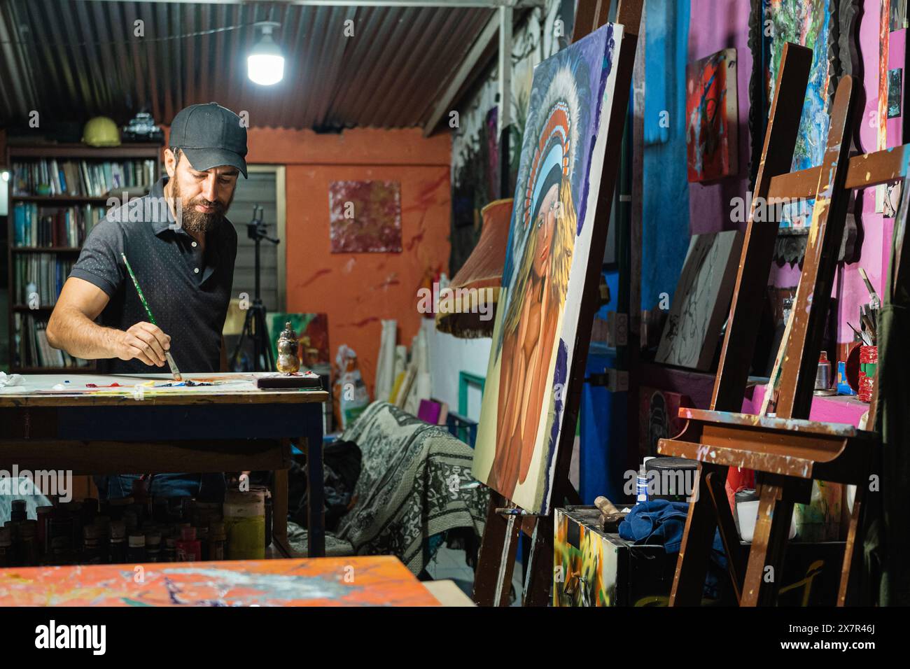 A focused Latin American artist is painting a colorful canvas in his ...