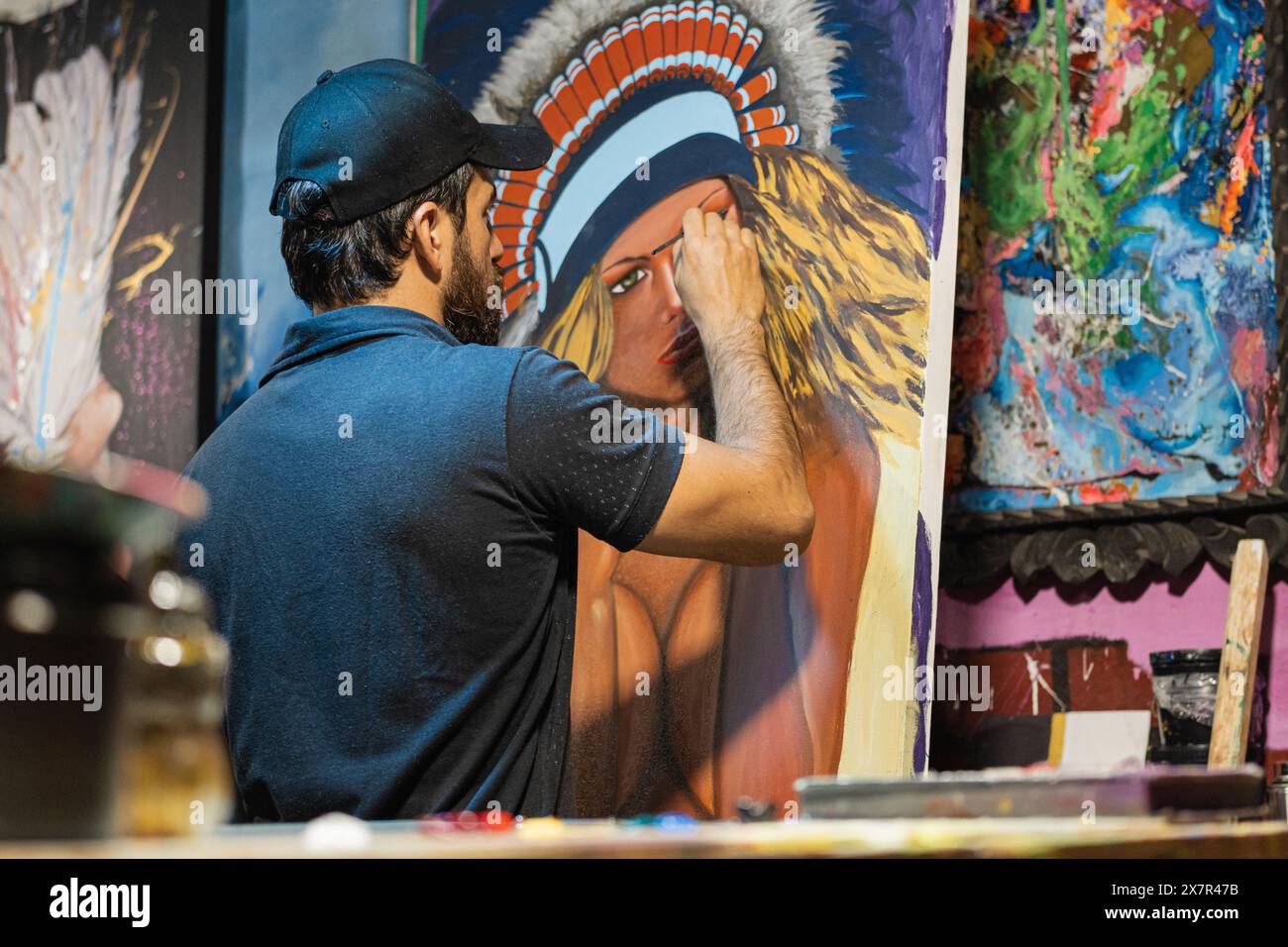 Side view of a Latin American artist working on a vibrant painting in ...
