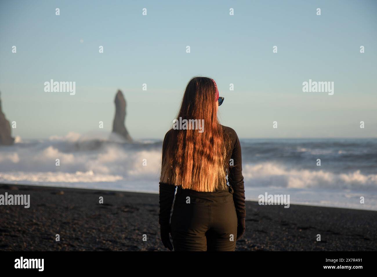 A woman gazes at towering sea stacks while standing on Iceland iconic ...