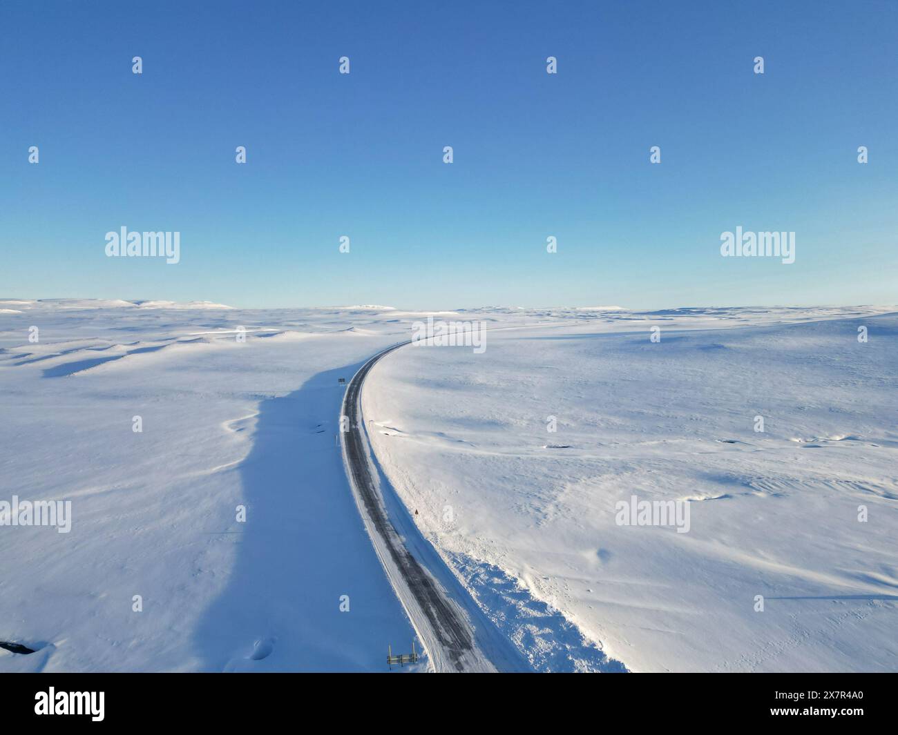 An aerial view of a lone road curving through a vast, snow-covered ...