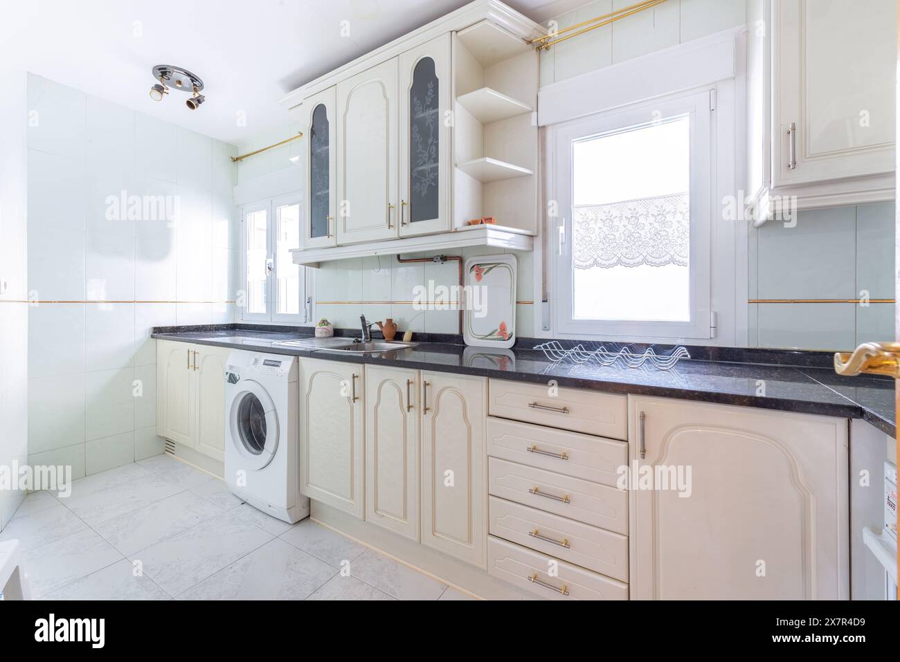 A sunlit, vacant kitchen with cream cabinets, black countertops, and ...