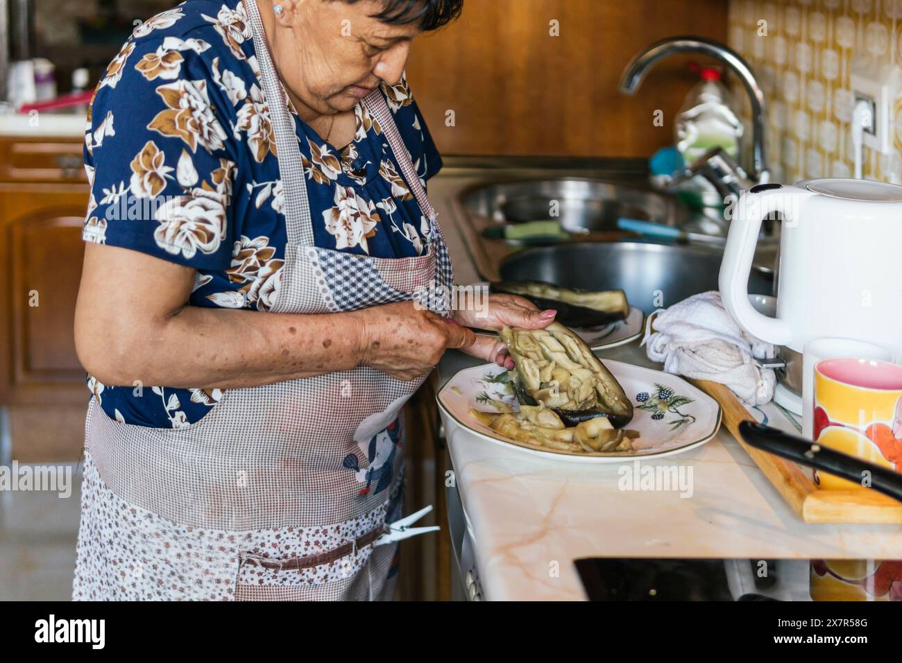 A senior woman is pictured at home cooking, carefully preparing ...