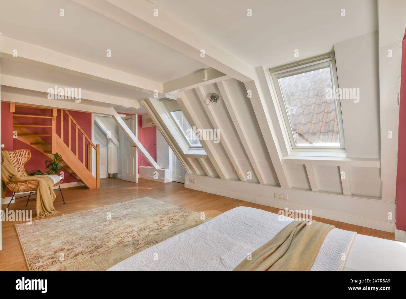 A spacious and airy attic room featuring exposed white beams, wooden ...