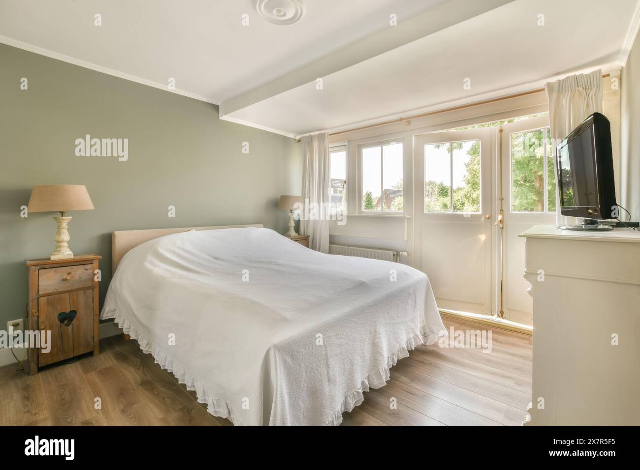 A well-lit cozy bedroom with a large bed, hardwood floors, and green ...