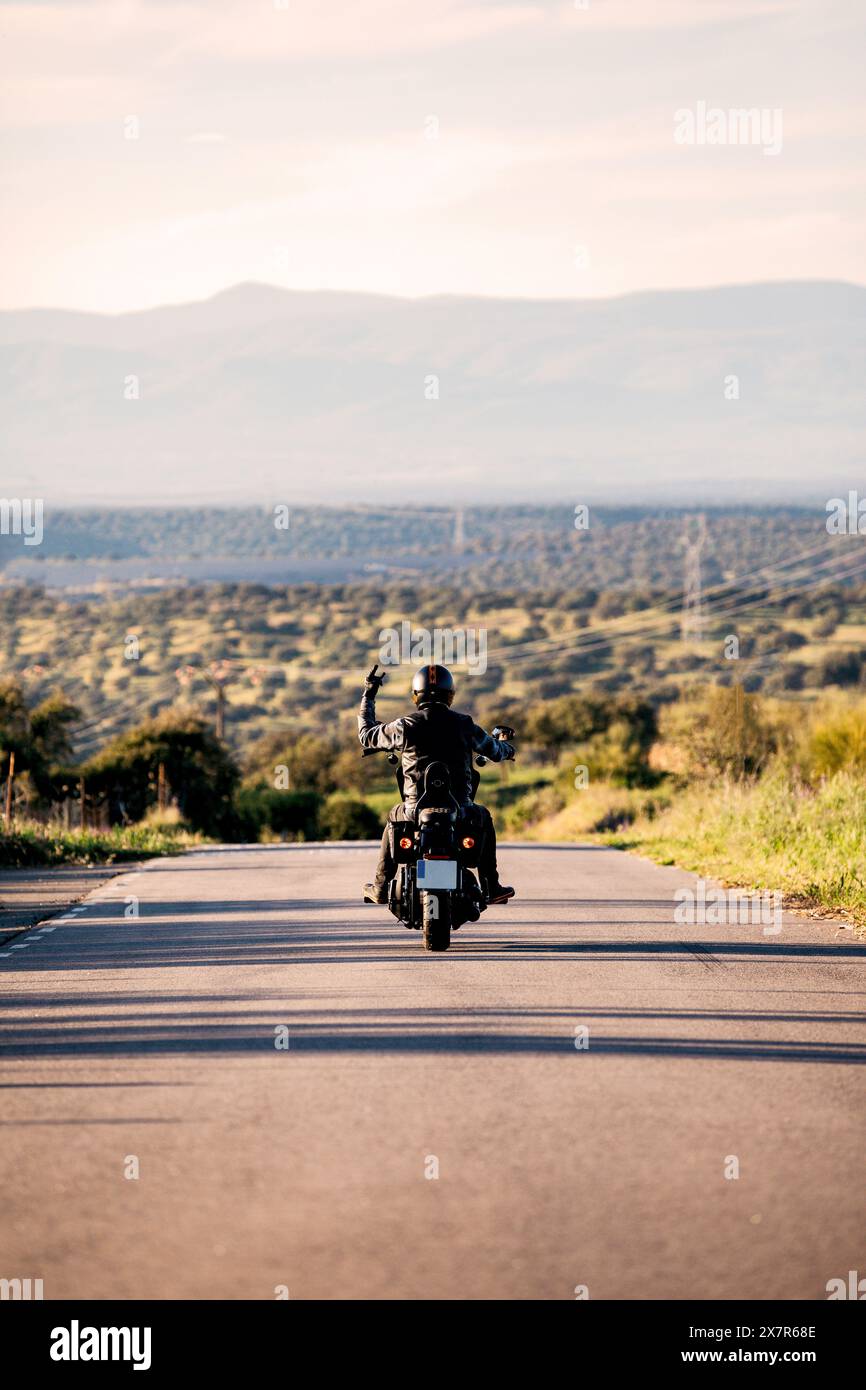 Back view of unrecognizable motorcyclist raises a peace sign while ...