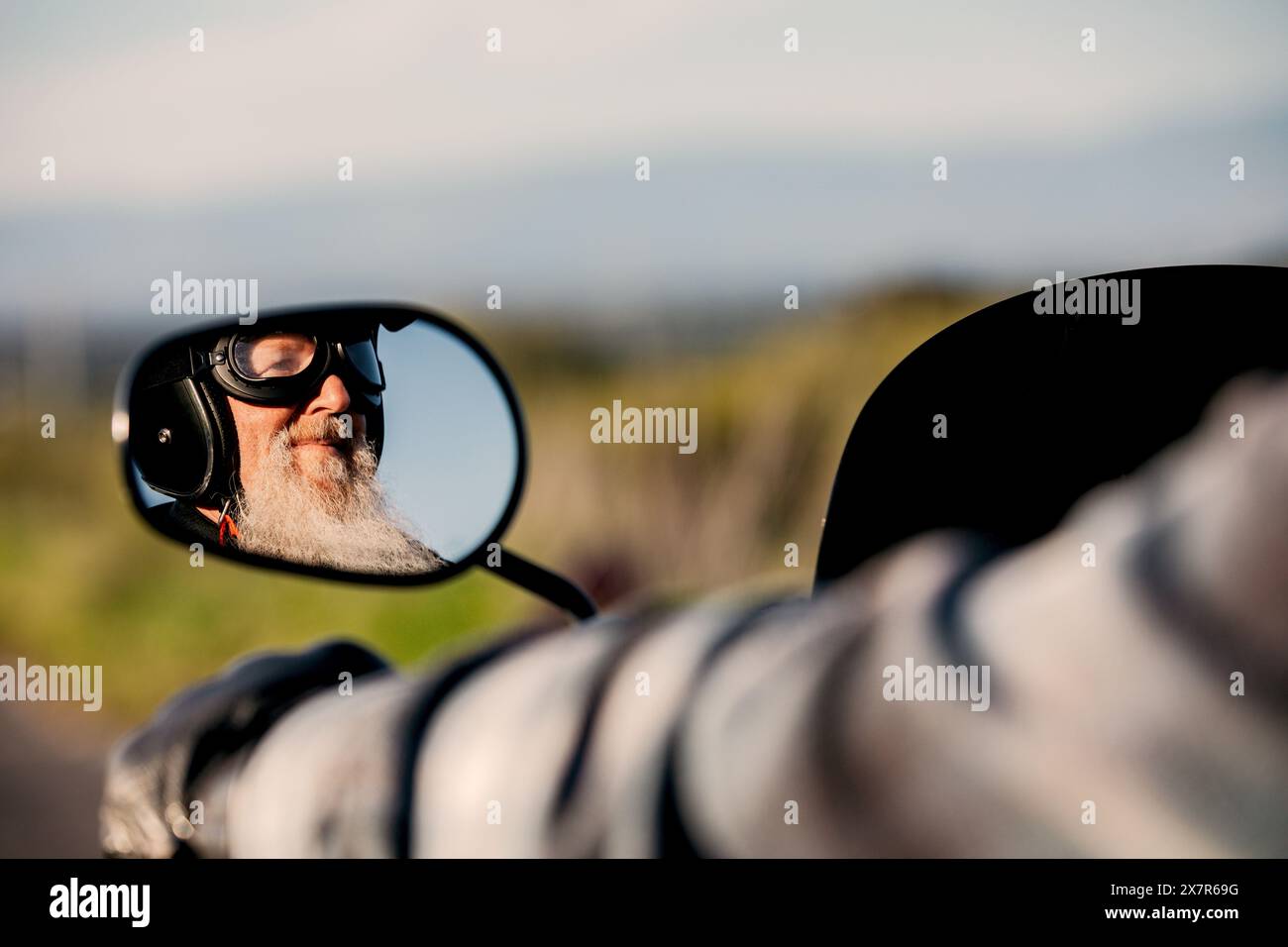 A senior male motorcyclist's reflection captured in the side mirror ...