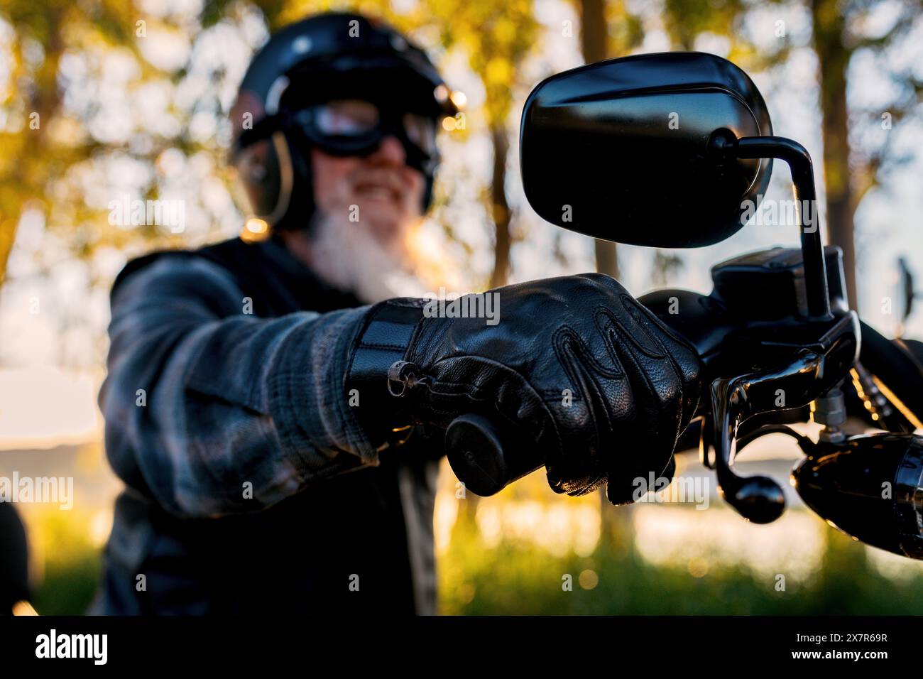 A mature male motorcyclist with a beard wearing a helmet and goggles ...