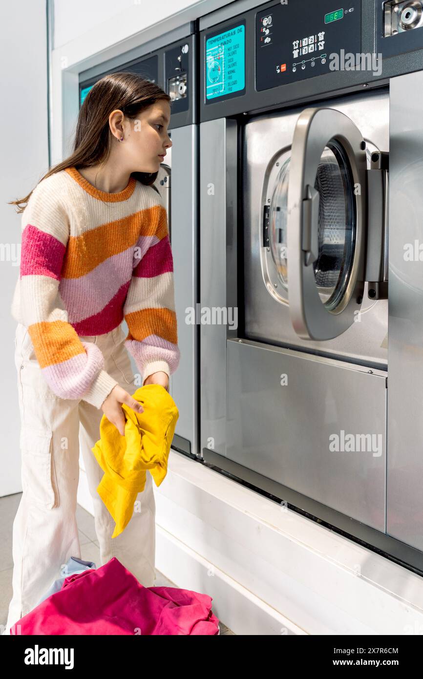 A preteen girl is sorting clothes beside a washing machine in a clean ...