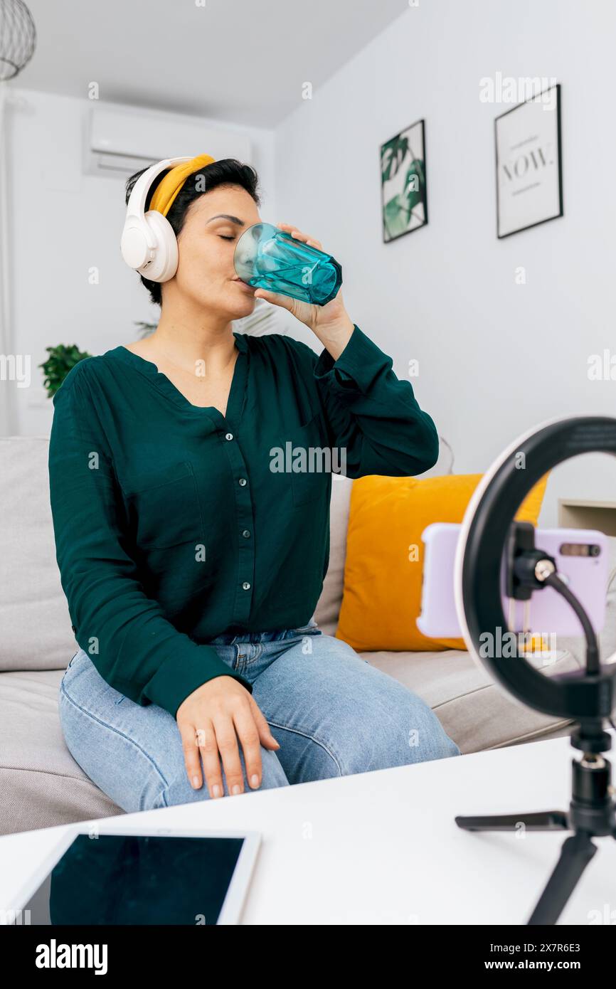 A female influencer enjoys a refreshing drink while recording a podcast ...