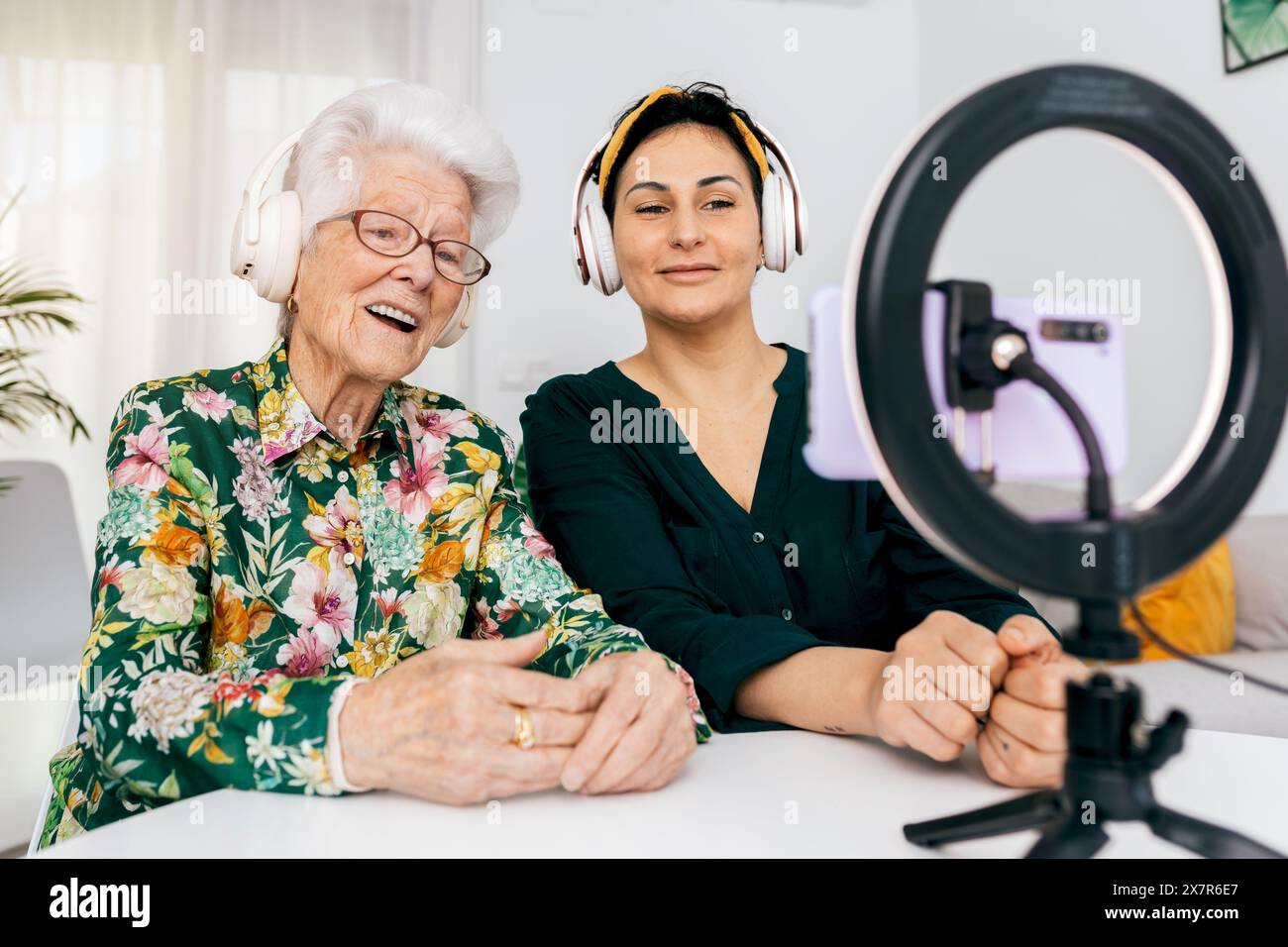 A young influencer and an elderly woman are seated at a desk, recording ...