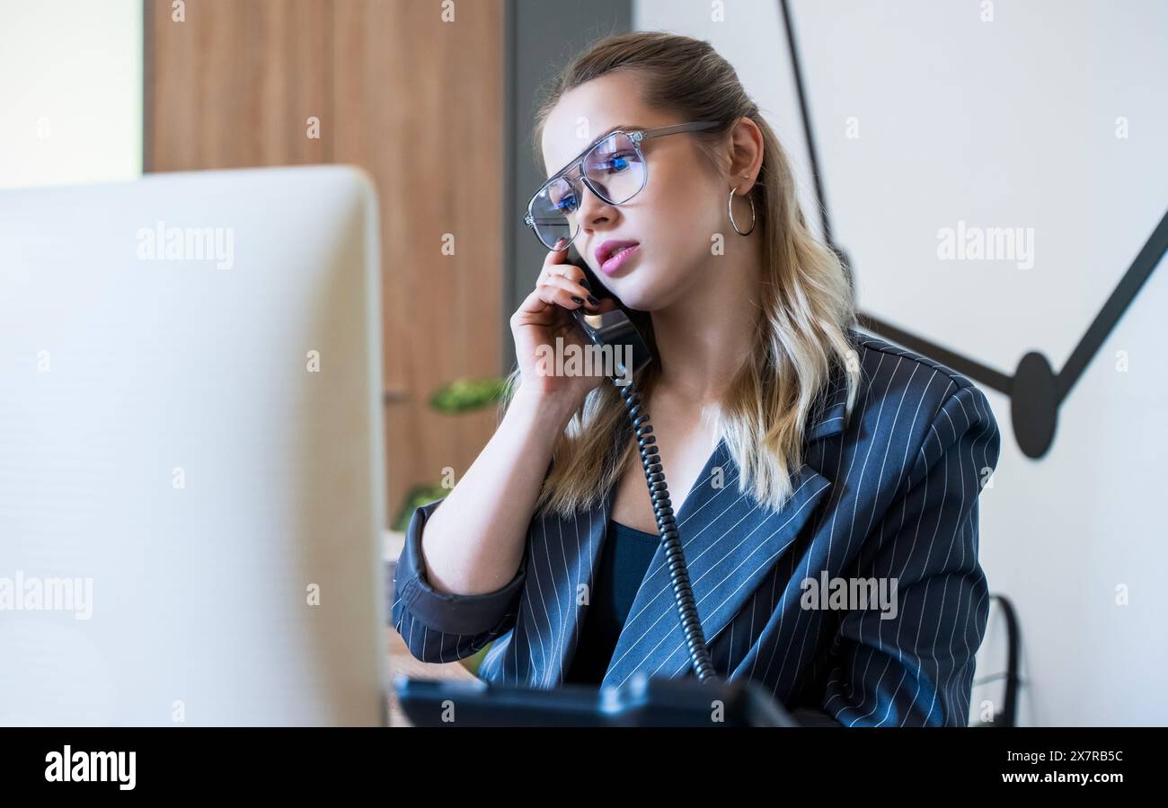 Pretty girl in glasses and formal suit in office talking on phone. An ...