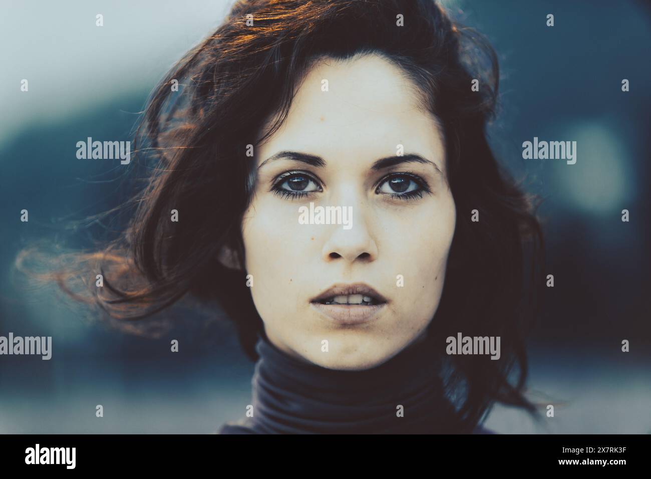 young woman with tousled hair gazes pensively. Her expressive eyes and ...
