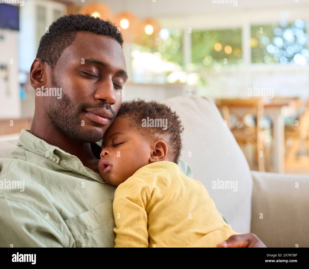 Family Shot With Father Cuddling Baby Daughter Sleeping On Sofa At Home ...