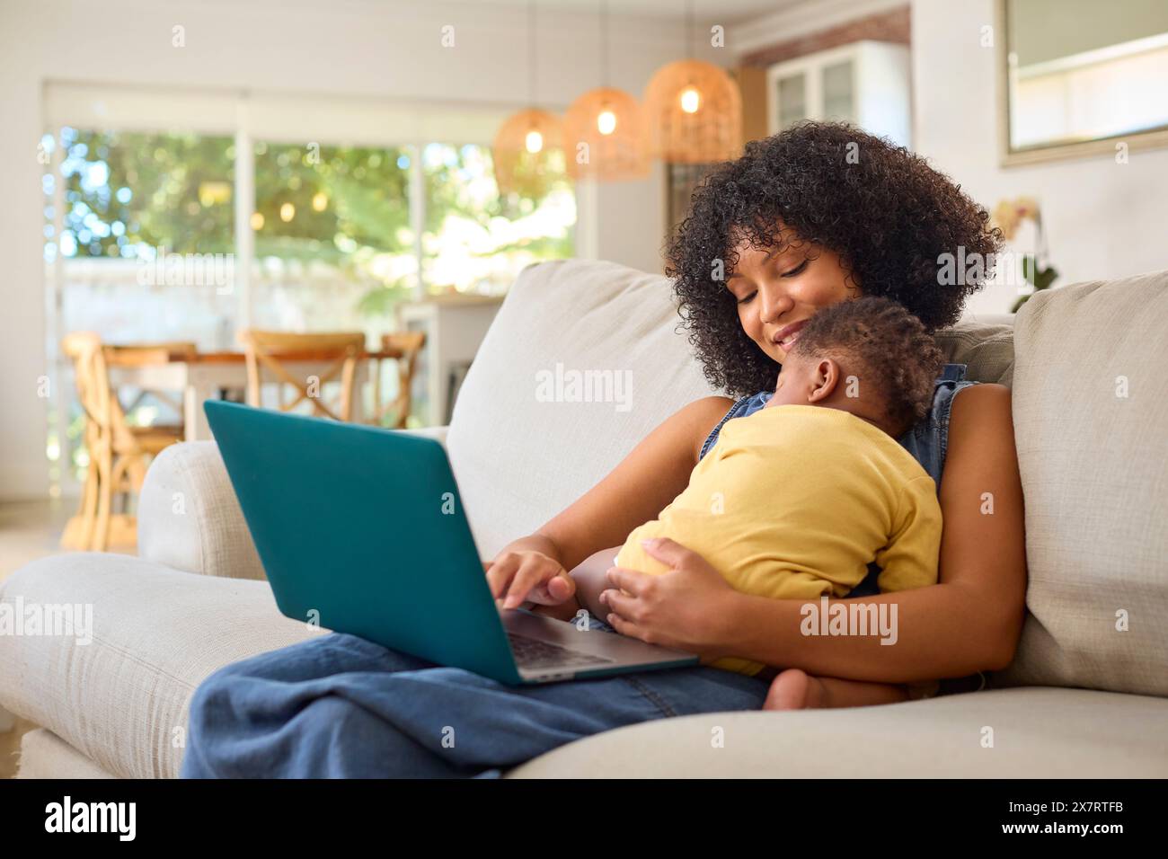 Family With Mother Working On Laptop Cuddling Sleeping Baby Daughter On ...