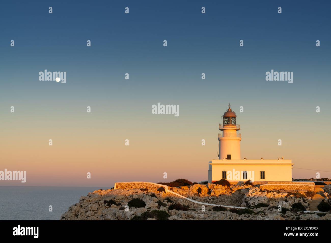 A vertical view of the Cap de Cavalleria Lighthouse on Menorca at sunset with a full moon rising ...