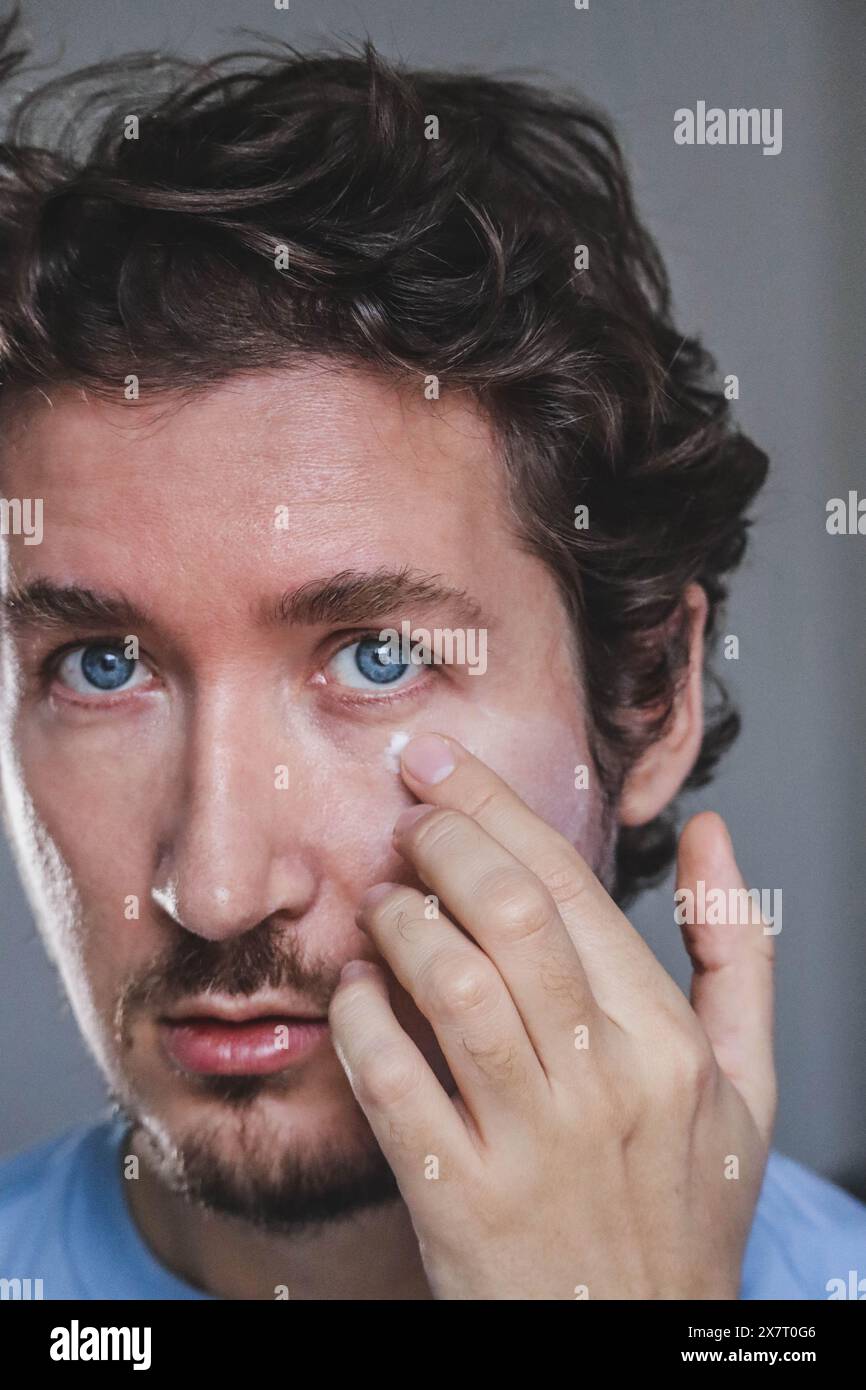 Handsome young man applying cream on his face Stock Photo - Alamy