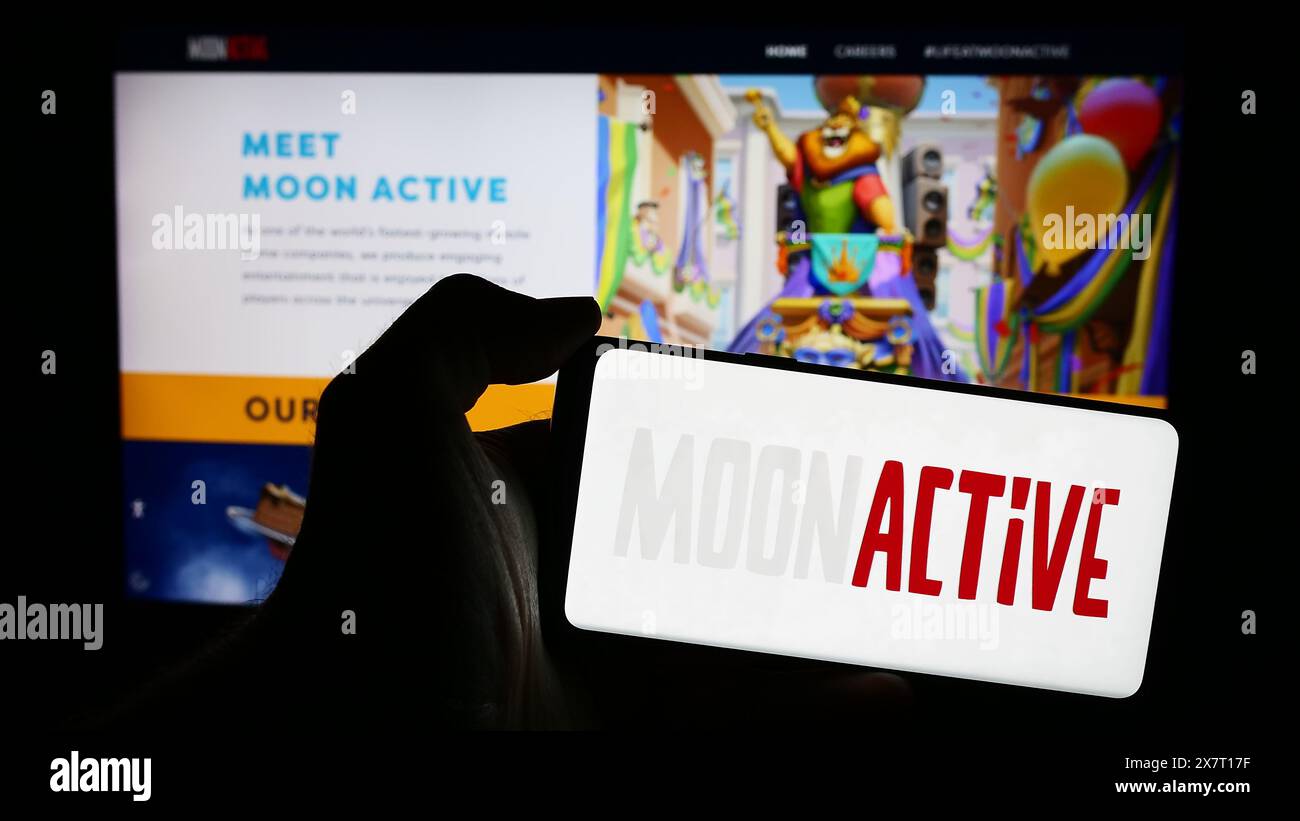 Person holding mobile phone with logo of Israeli mobile games company Moon Active Ltd. in front ...