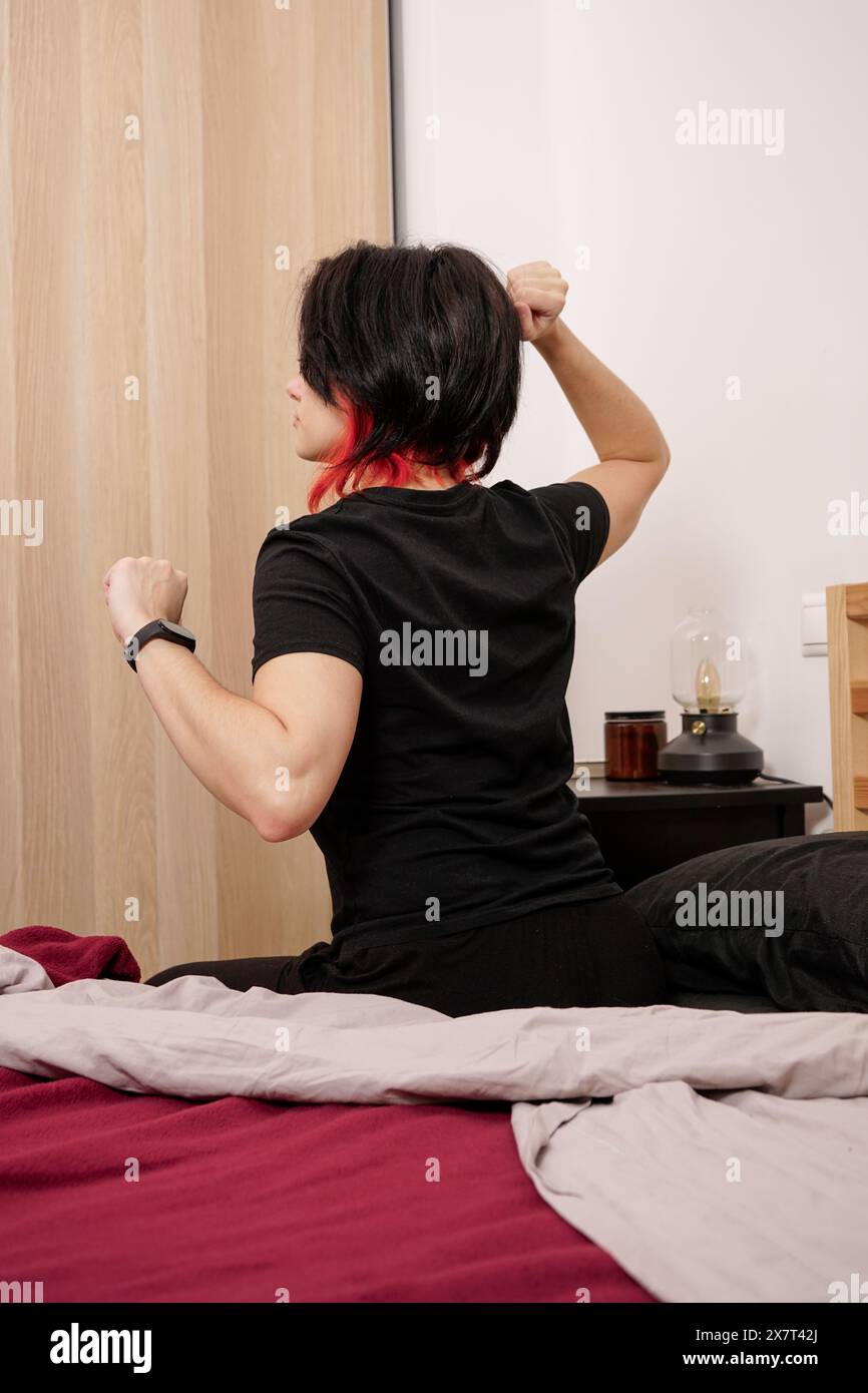 Black-haired white person stretching getting up from bed, starting ...