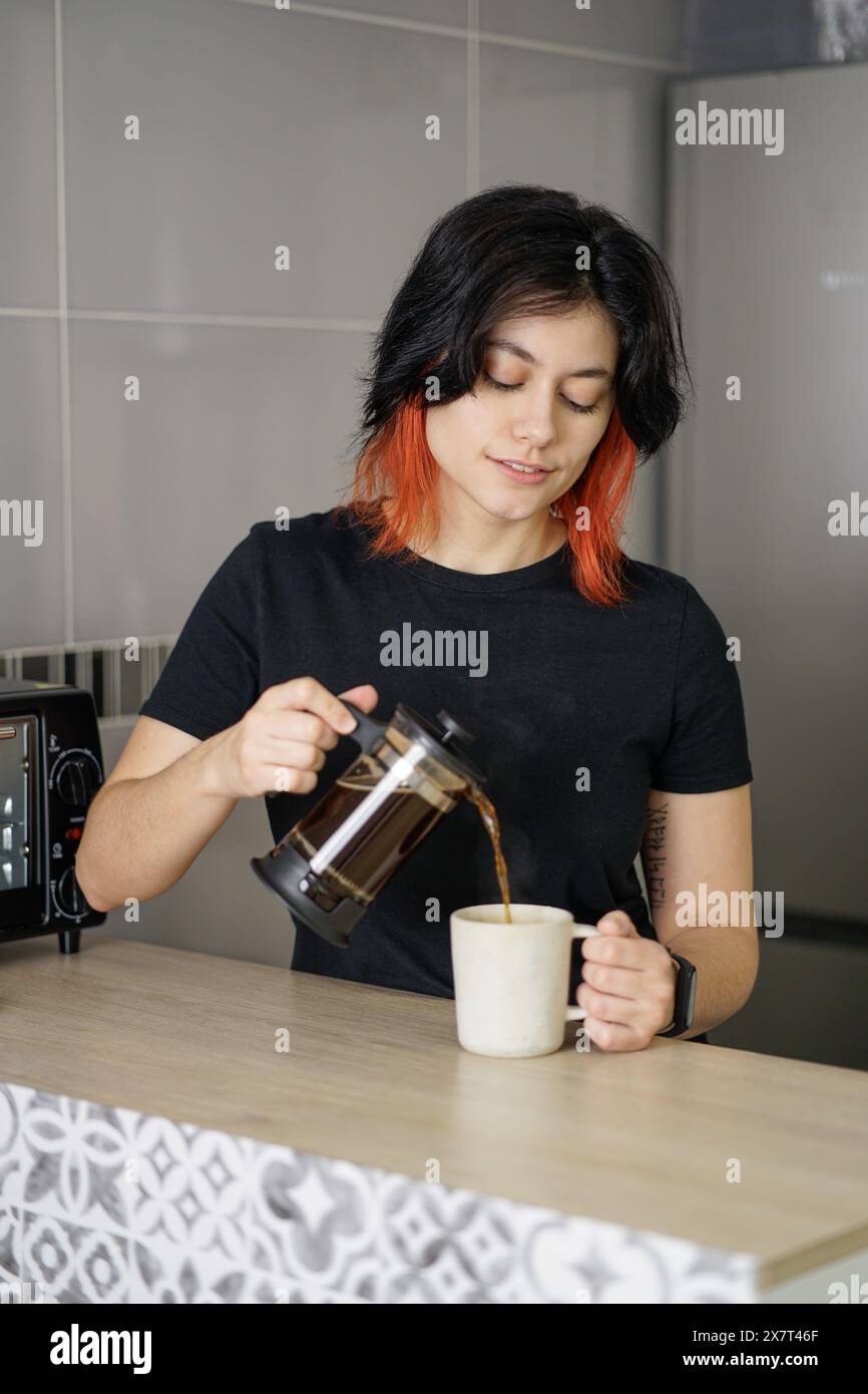 Black-haired white person serving coffe from a french press to a mug ...