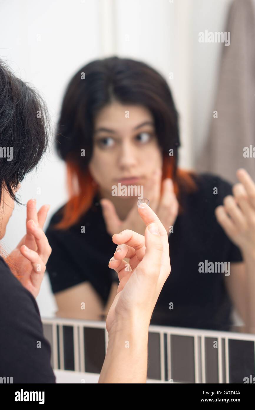 White person putting on contact lenses while looking at themselves in ...