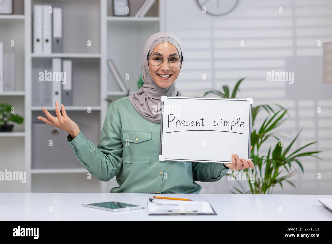 Smiling teacher in hijab holding whiteboard with 'Present Simple ...