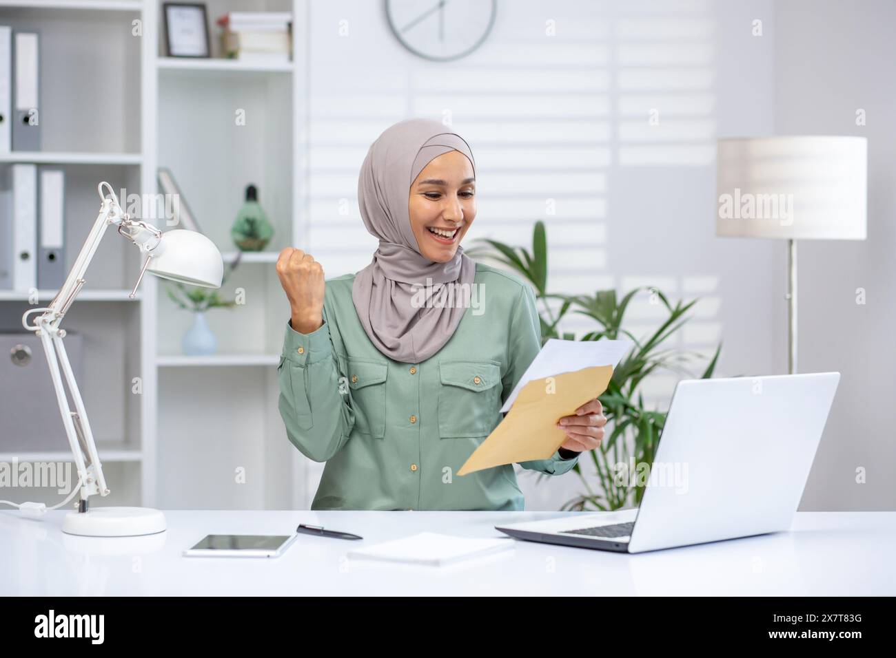 Happy woman in hijab celebrating while reading a letter at her office ...