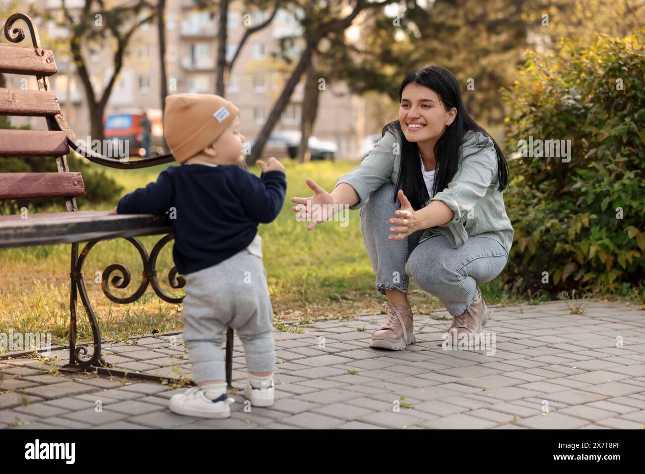 Little baby making his first steps to mother in park, back view. Happy ...