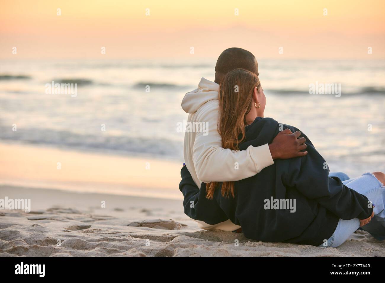 Rear View Of Casually Dressed Loving Young Couple Sitting On Beach