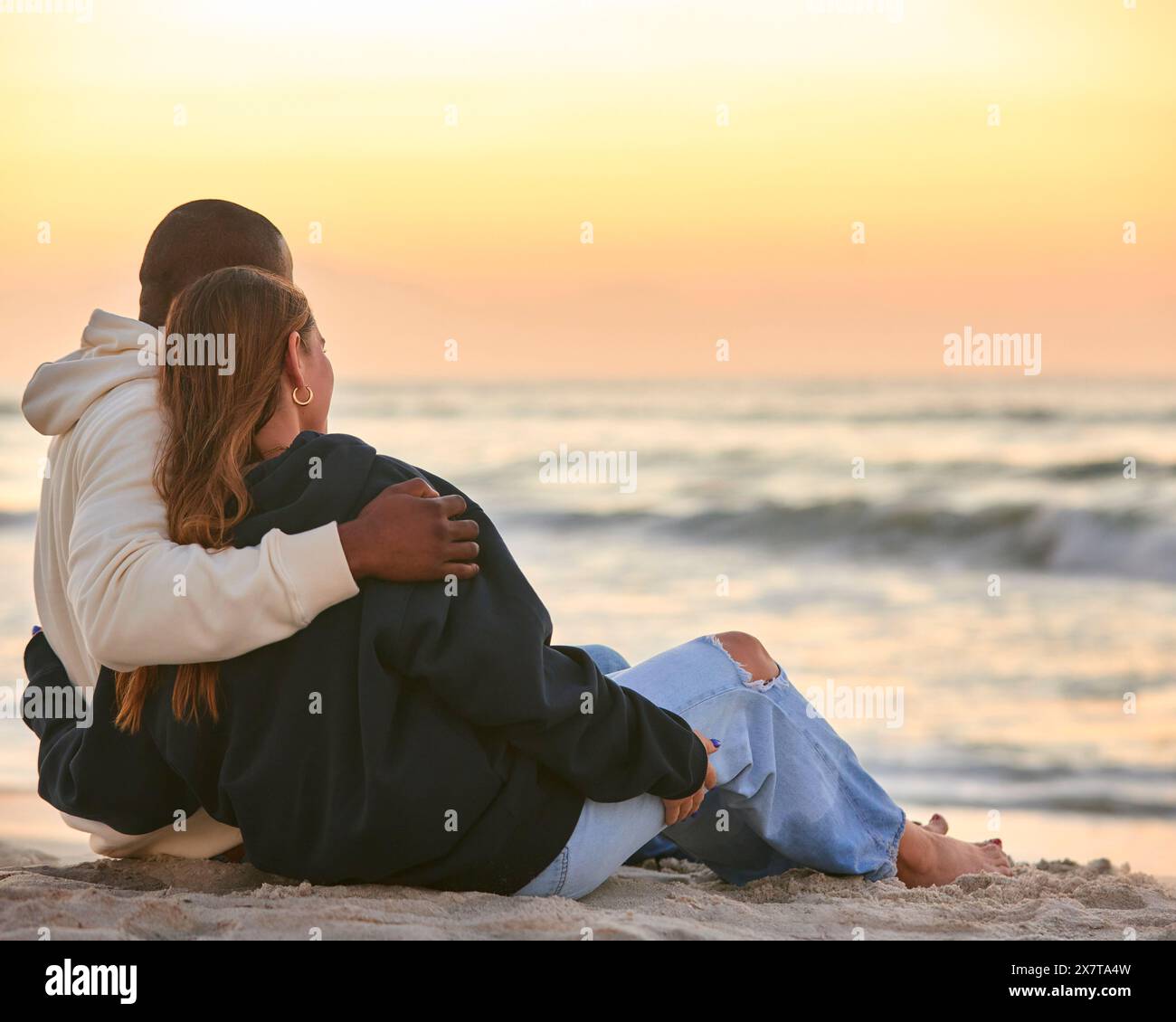 Rear View Of Casually Dressed Loving Young Couple Sitting On Beach