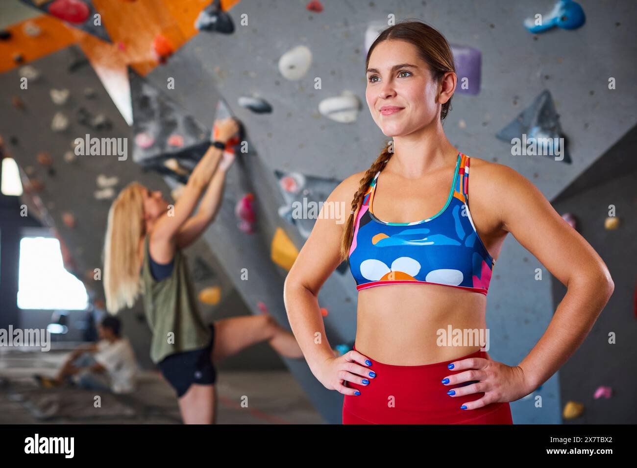 Portrait Of Female Coach In Front Of Climbing Wall At Indoor Centre With Climber In Background ...