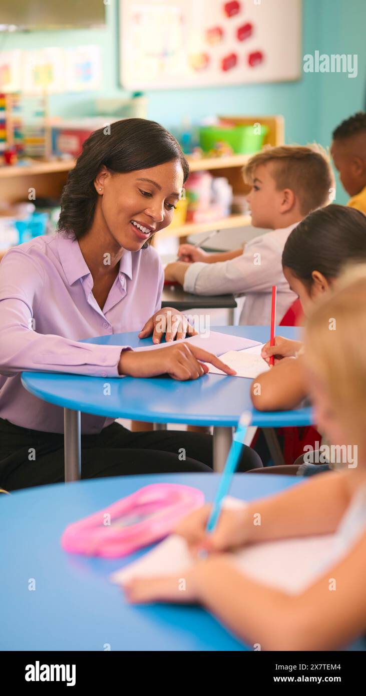 Female Primary Or Elementary School Teacher Helping Students At Desks ...