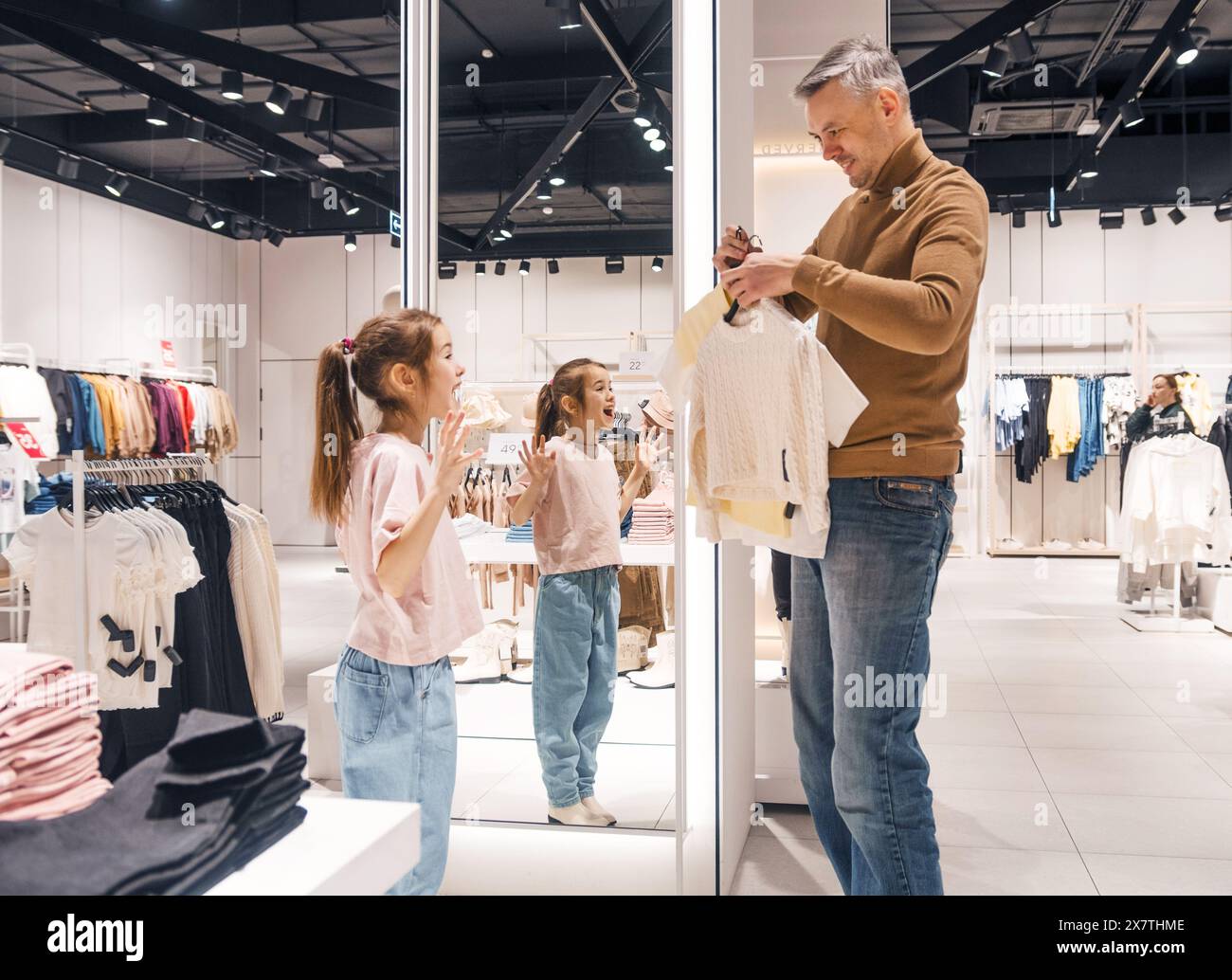 A father helps his young daughter choose clothes in a modern retail ...
