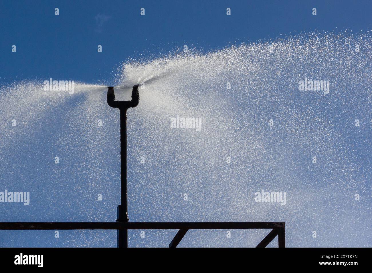 two water sprinklers spraying water with a clear blue sky as a ...