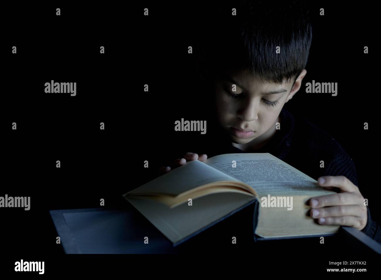 Latino child concentrating on reading a large book with a black ...