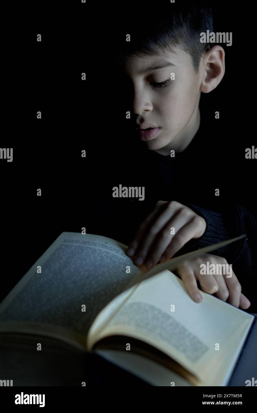 intelligent latino child turning the page of a book he is reading in a ...