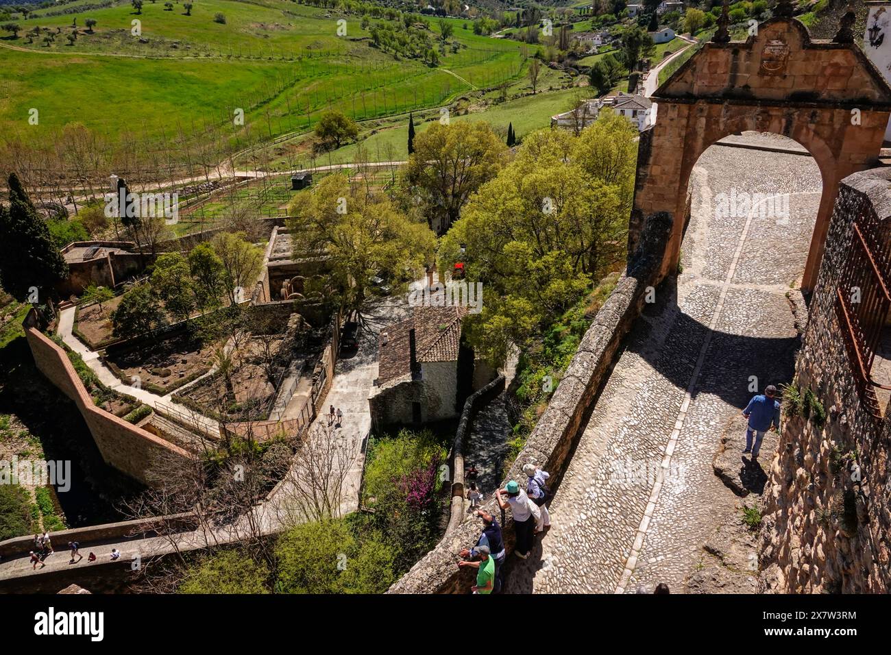 Tourists stand on the Old Bridge near the Felipe V arch looking down ...