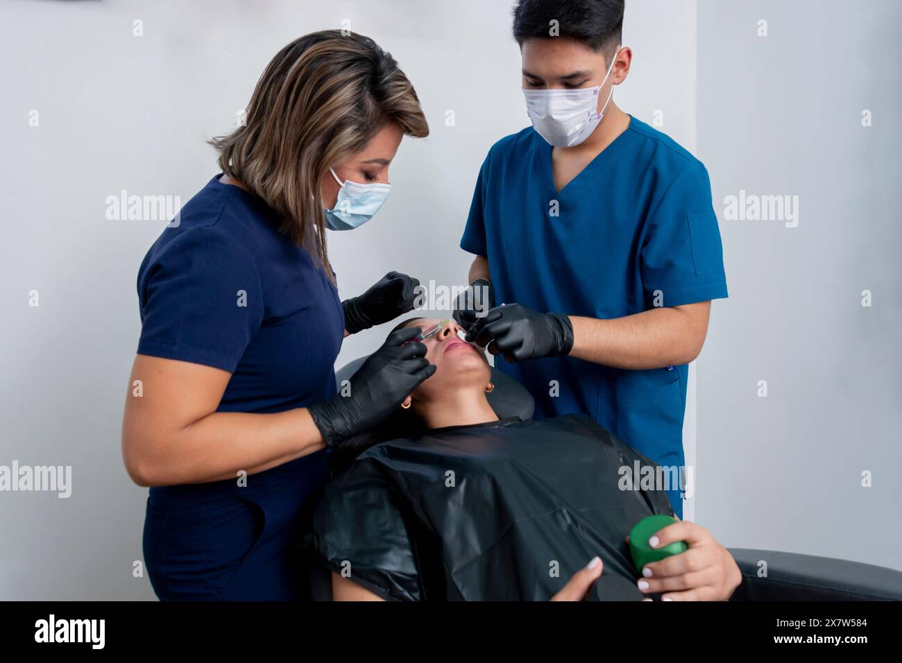 Female doctor and her assistant applying botox to the lips of a young ...