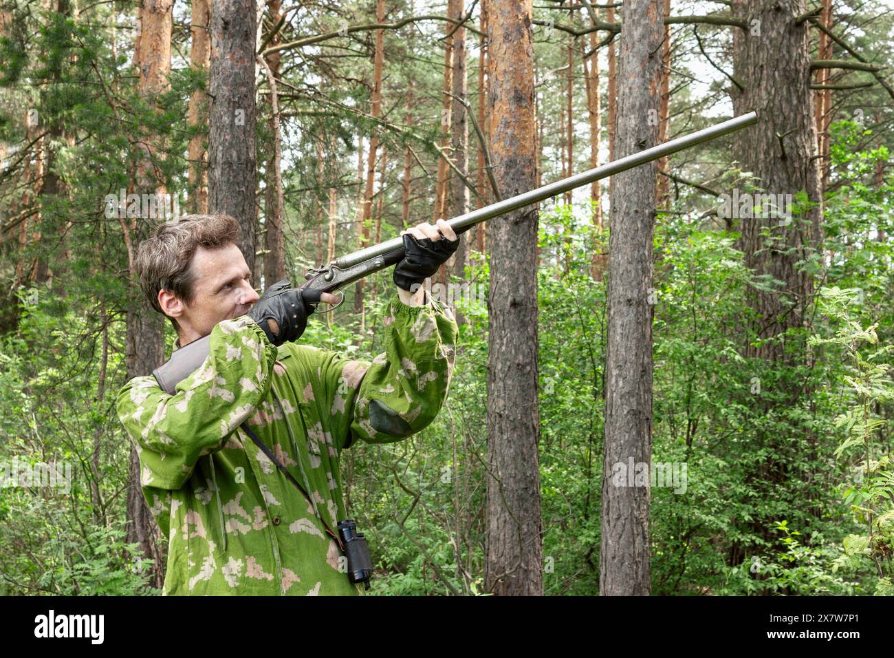 Shooter with an old gun and in camouflage in the forest while hunting ...