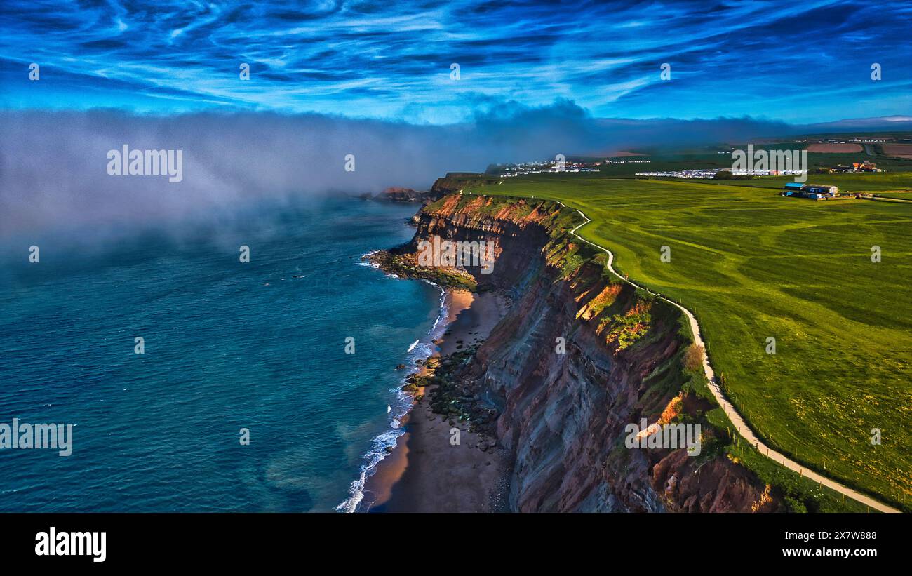 Aerial view of a dramatic coastal cliff with green fields on top, a ...
