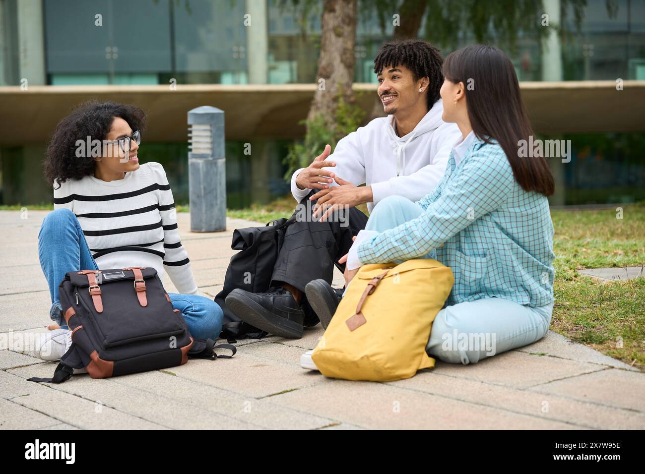 Three young people sitting on the ground with backpacks Stock Photo - Alamy