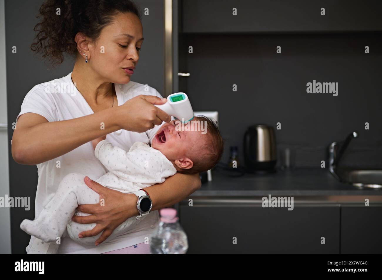 Mother measuring the body temperature of her baby, using contactless ...