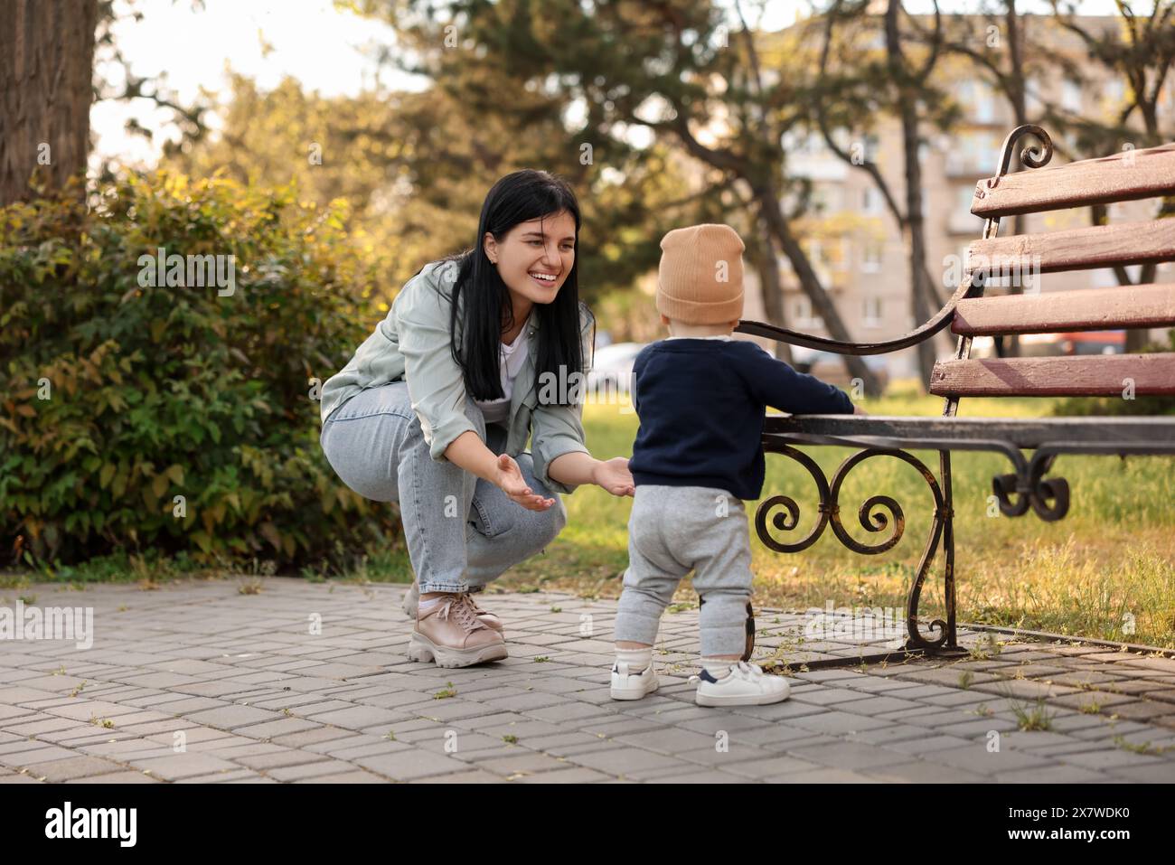 Little baby making his first steps to mother in park, back view. Happy ...