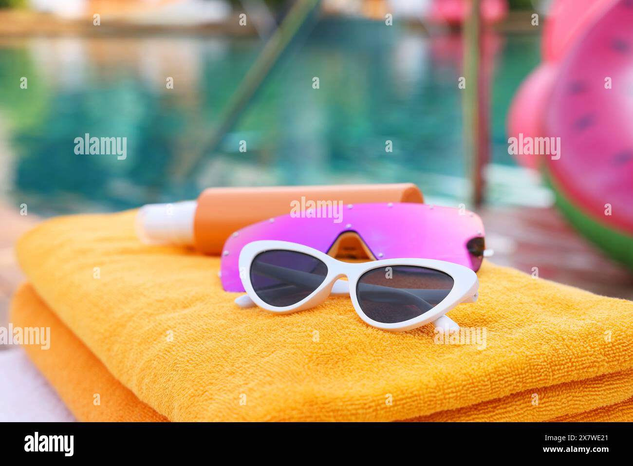 Beach towels, sunglasses and sunscreen on sunbed near outdoor swimming ...